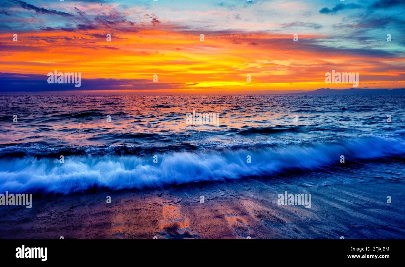 A Colorful Ocean Sunset As A Wave Rolls to Shore Stock Photo - Alamy