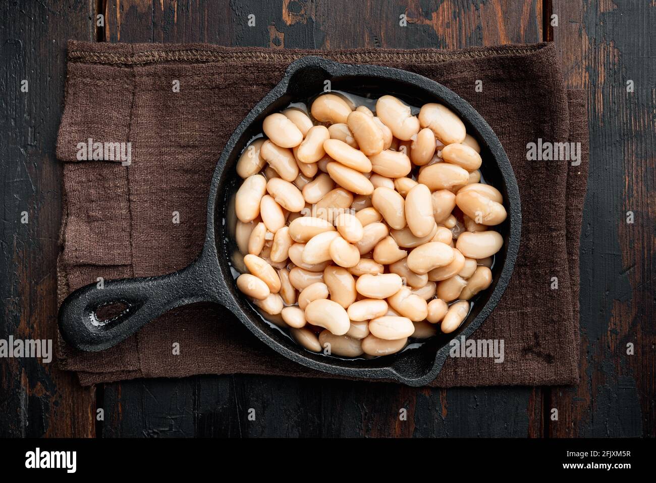White canned beans set, in cast iron frying pan, on old dark wooden ...