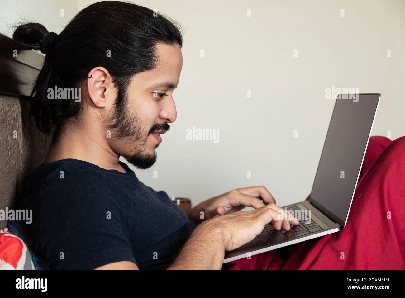 Young latin man working on bed at home with a computer on his legs ...