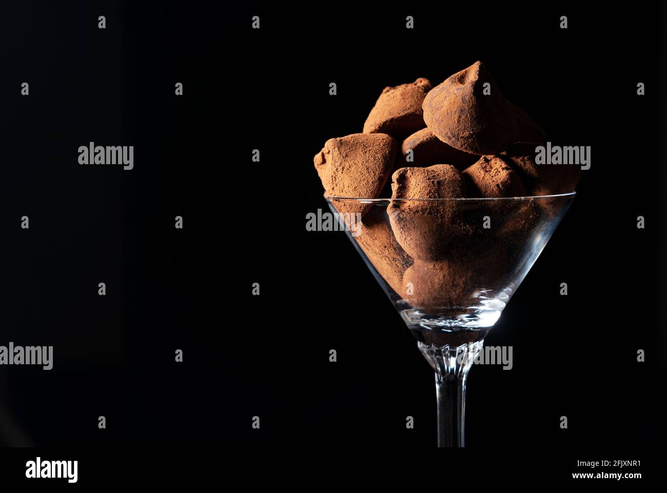 Chocolate truffles in a cocktail glass on a black background with copy ...
