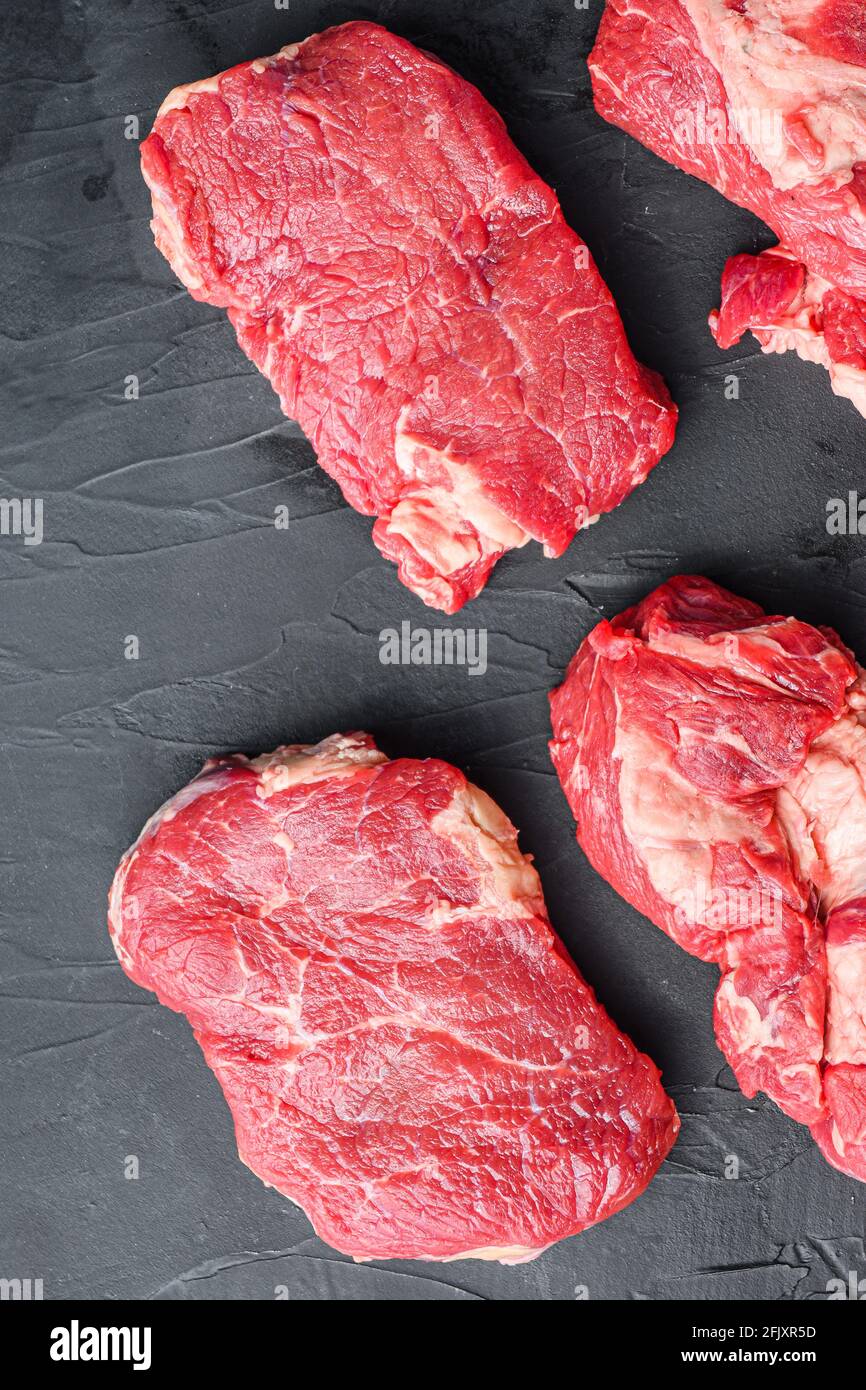 Two raw organic rump beef steaks, side view on black textured table ...
