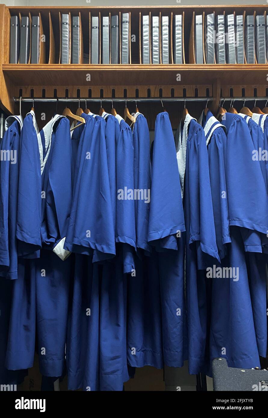 Group of blue choir robes hung up on a rack with the choir books inside ...