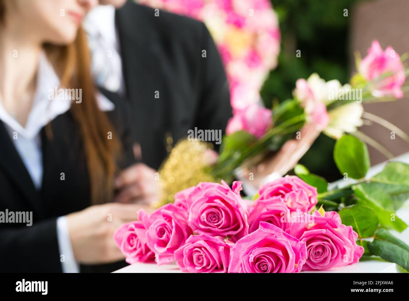 Mourning man and woman on funeral with pink rose standing at casket or ...