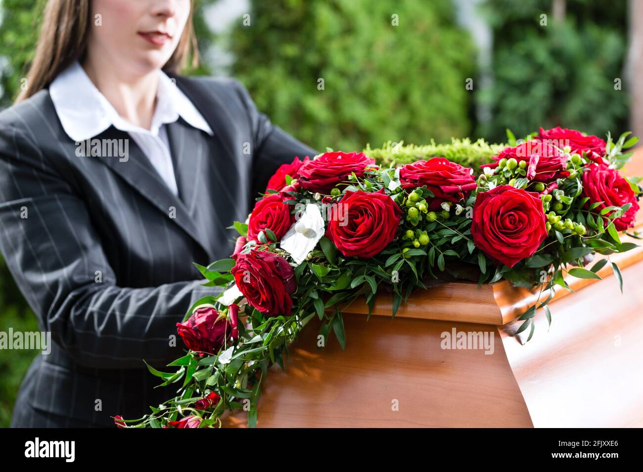 Mourning woman on funeral with red rose standing at casket or coffin ...