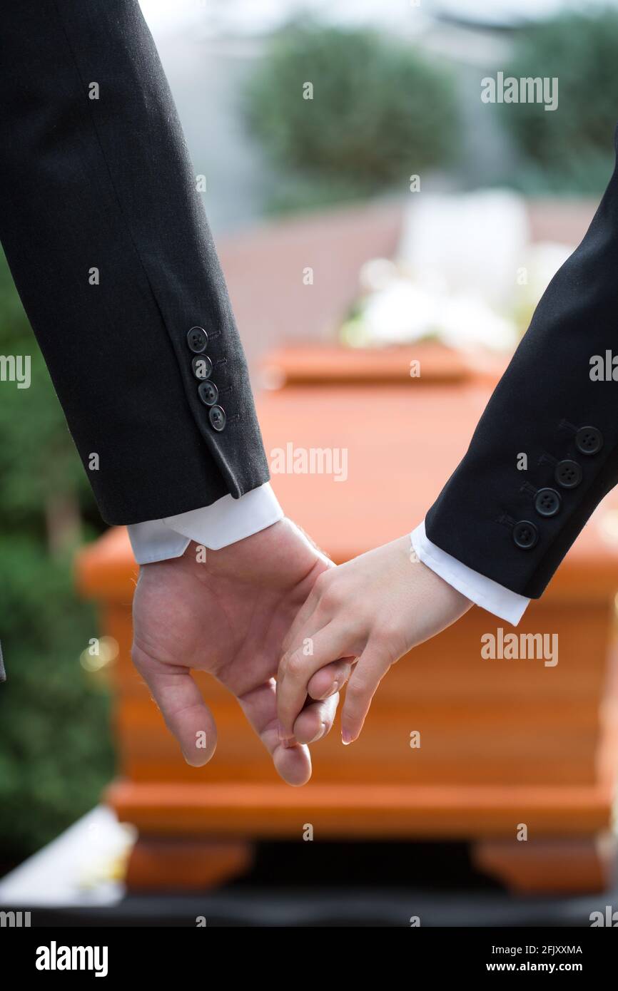 Religion, death and dolor - couple at funeral holding hands consoling ...