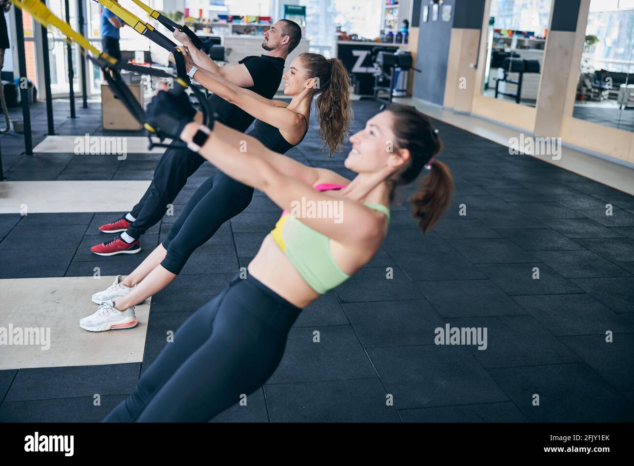Three athletes doing the back row exercise using suspension trainers ...