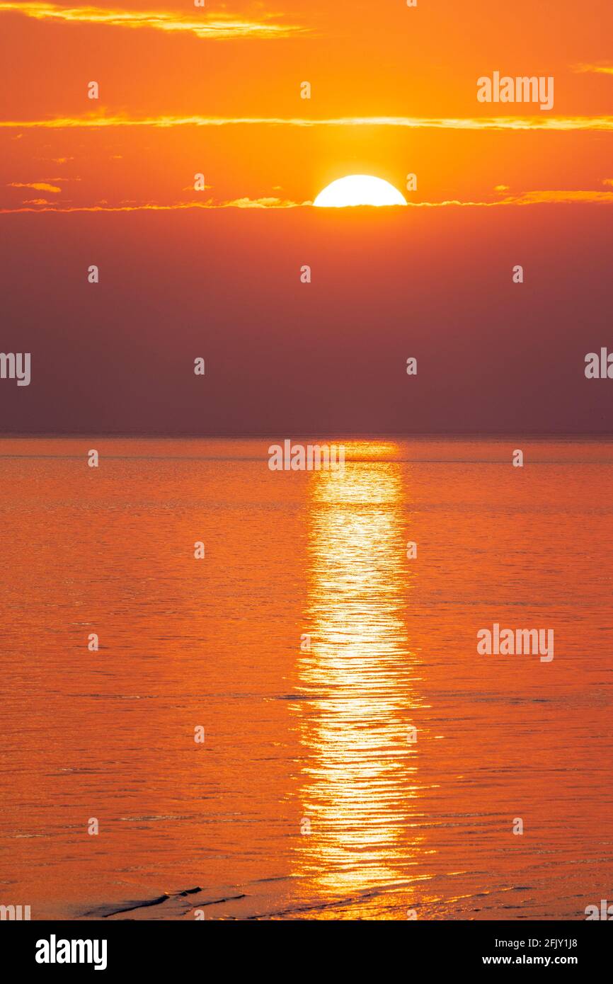 The sun rising over a layer of cloud on the horizon above the sea with ...