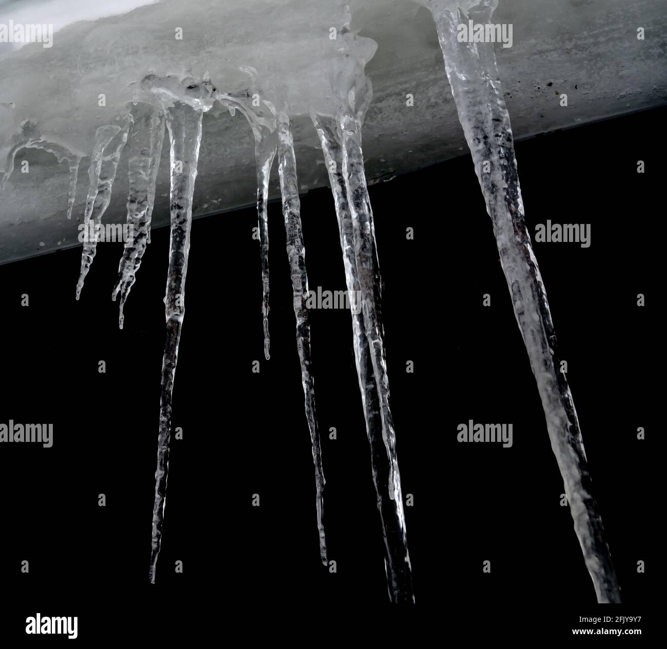 Long pointy icicles from frozen water hanging of the side of a roof ...