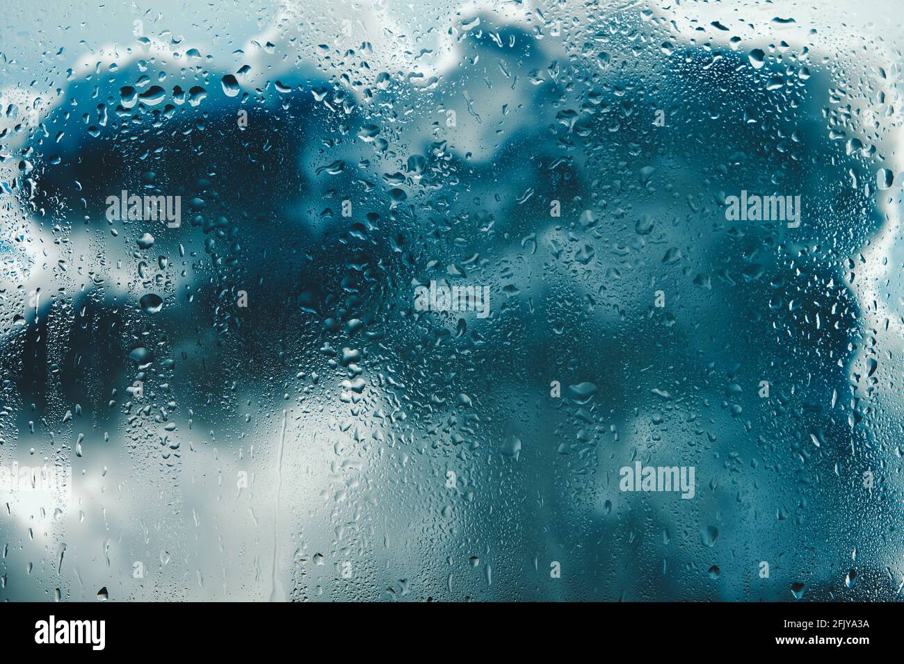 Wet, fogged glass in rain against background of blurred clouds in out ...