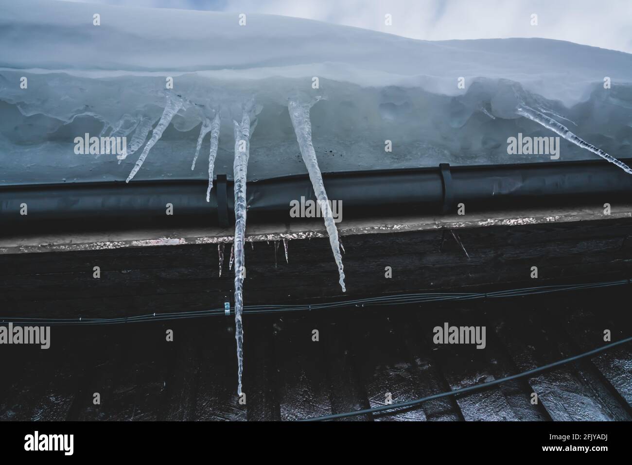 Long pointy icicles from frozen water hanging of the side of a roof ...