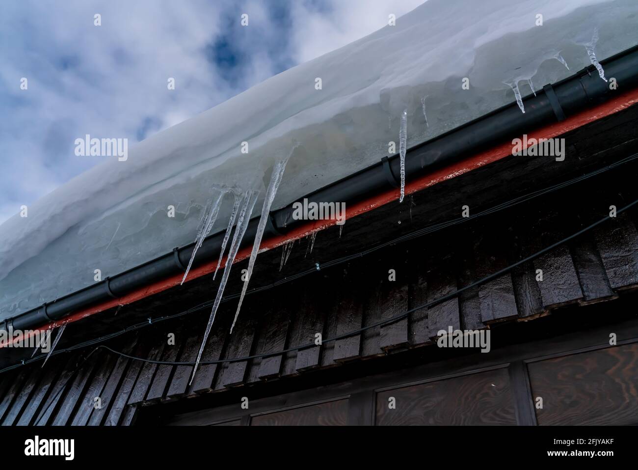 Long pointy icicles from frozen water hanging of the side of a roof ...