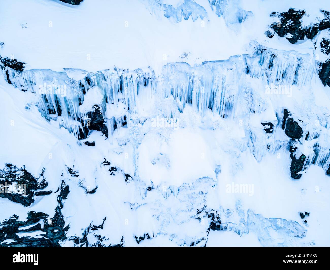 Massive long frozen icicles hanging of the side of a cliff on a ...