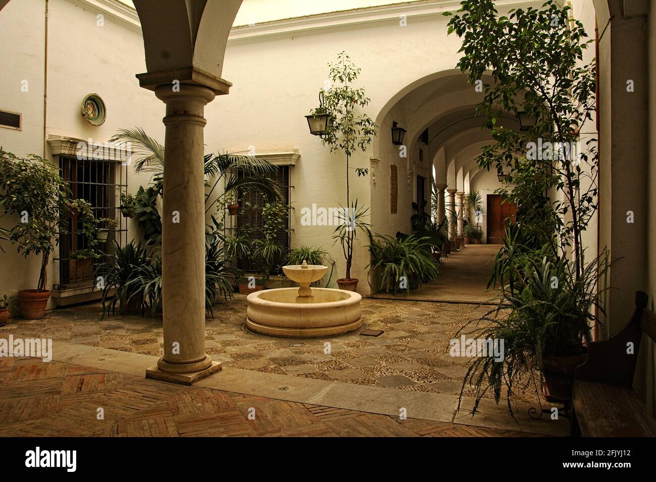 Interior of a building with columns, arches, plants and a fountain ...