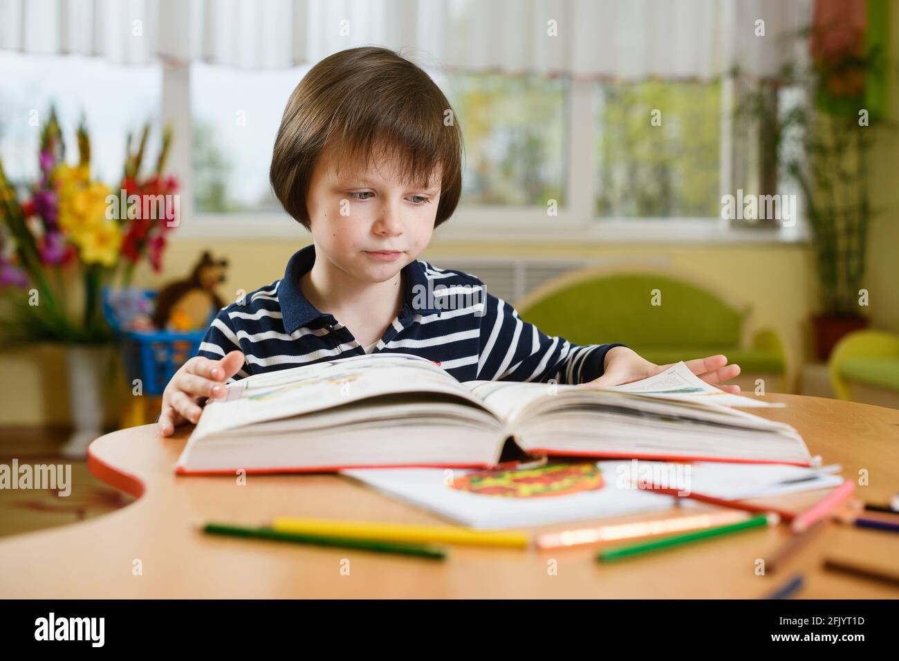 A preschool boy is reading a huge book. The book lies on the table ...