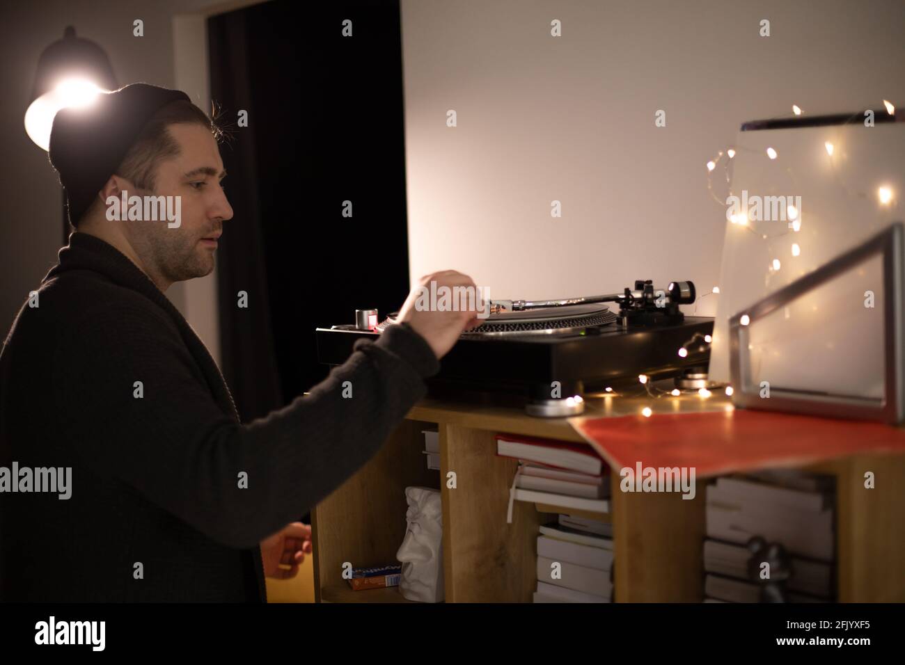 Young unshaven handsome hipster guy puts tonearm on vinyl record on ...