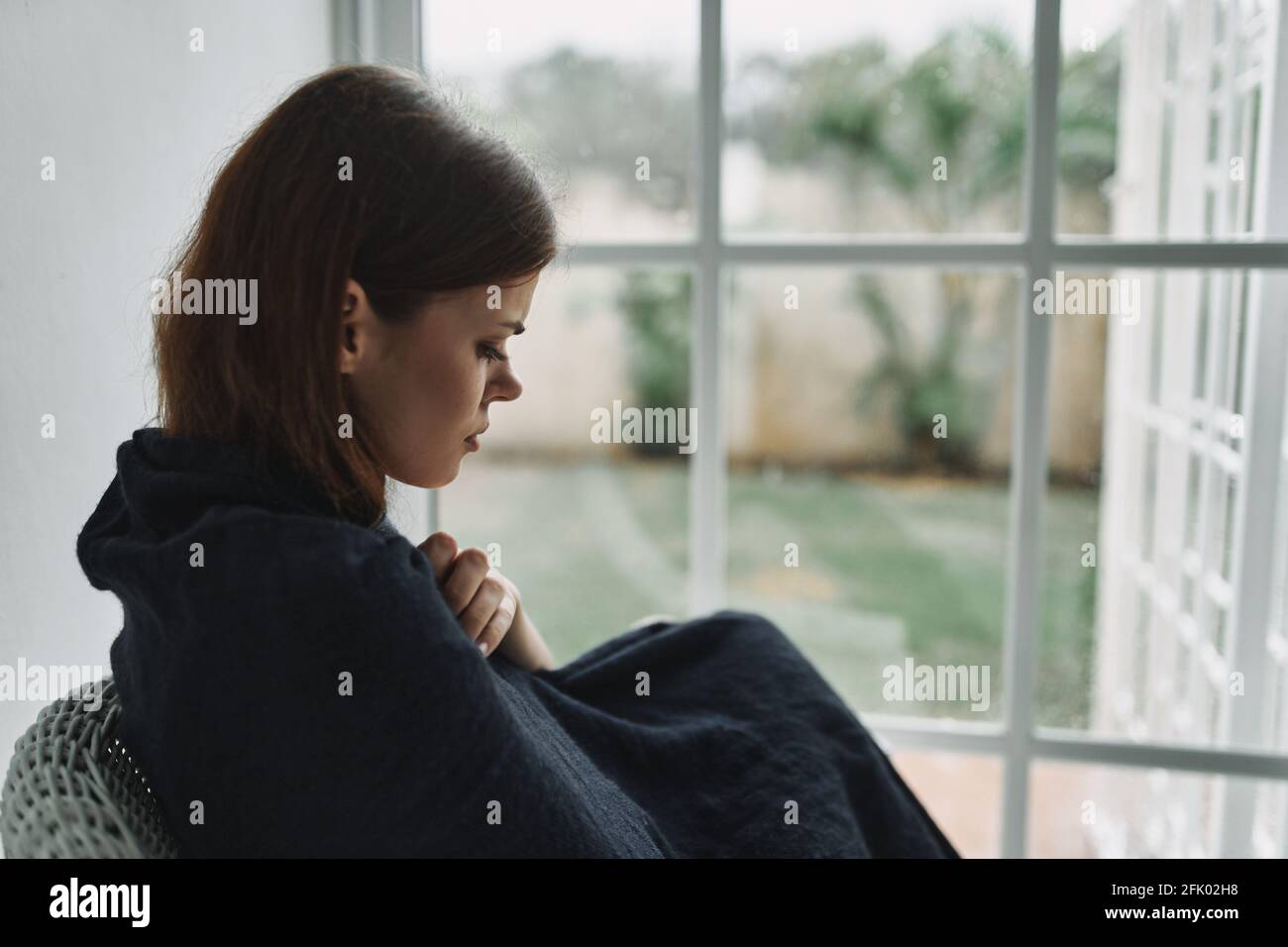 frozen woman sitting near the window covered with a blanket side view ...