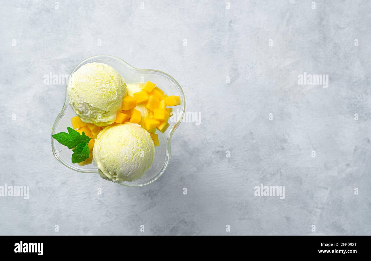 Two balls of mango ice cream and slices of fresh mango on a gray ...