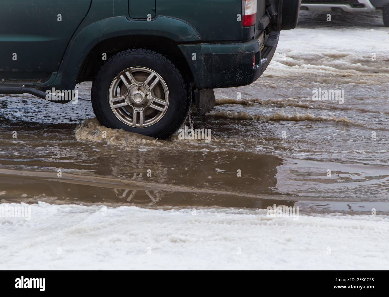 The wheel of a car driving through a deep puddle of melted snow ...