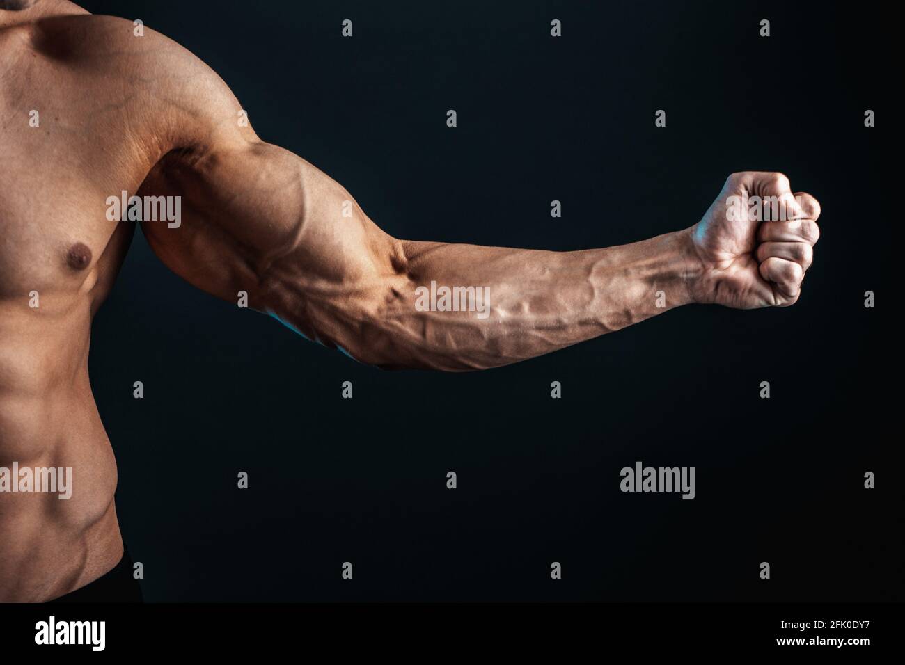 tense arm clenched into fist, veins, bodybuilder muscles on a dark ...