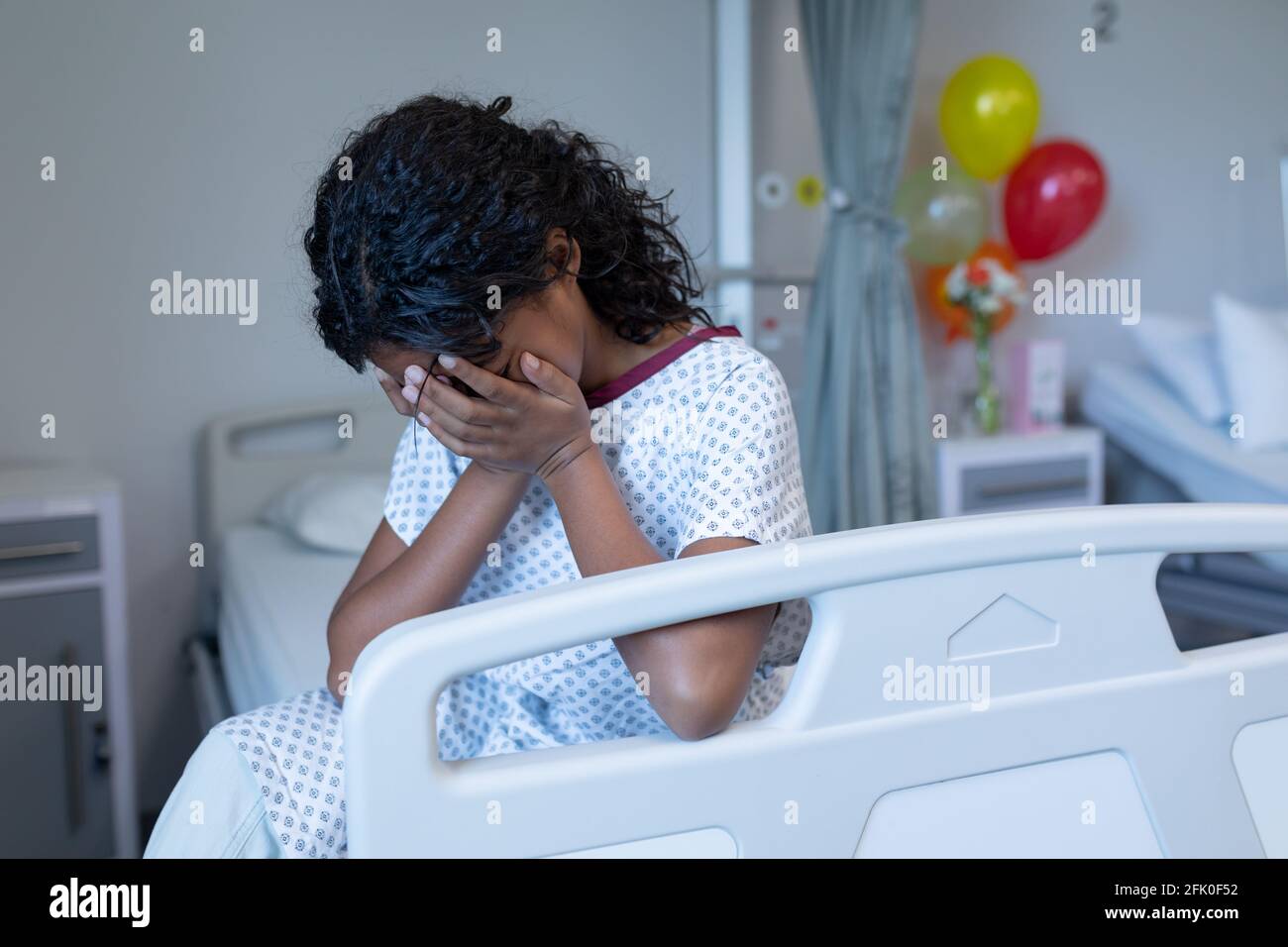 Sad sick mixed race girl sitting on hospital bed crying, with head in ...