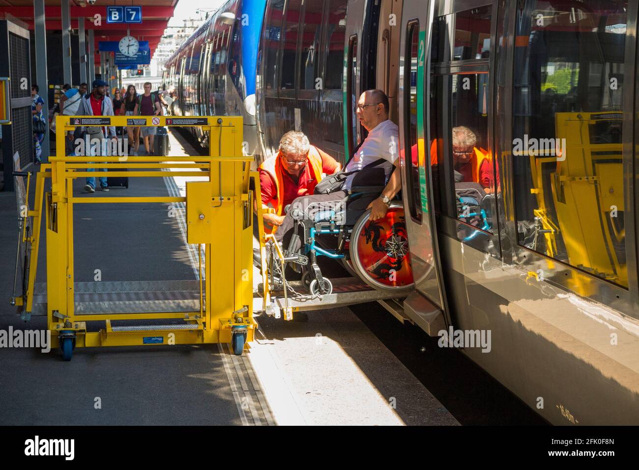 A Railway Worker Provides Help To A Disabled Passenger Alighting From The Train At Geneva