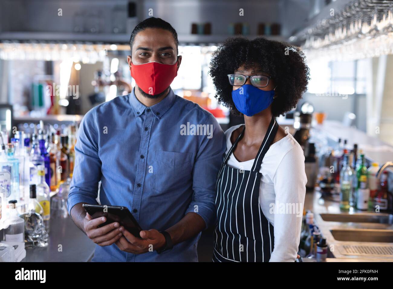 Diverse male and female baristas wearing face masks, looking at camera ...