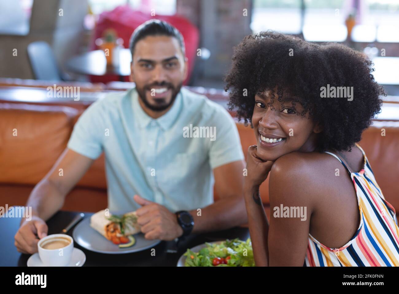 Smiling mixed race man and african american woman eating in restaurant ...