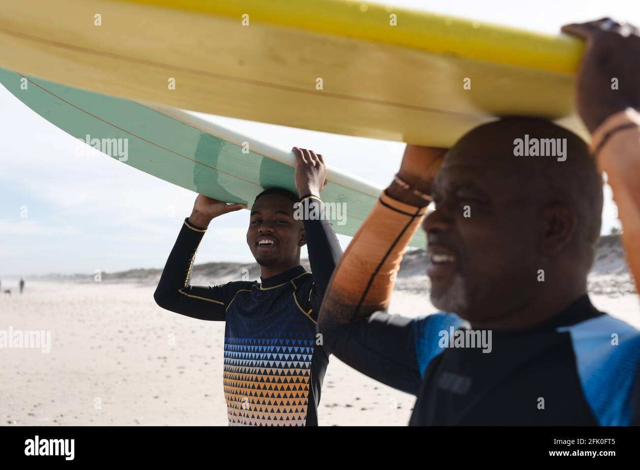 African american father and son carrying surfboards on their heads at ...