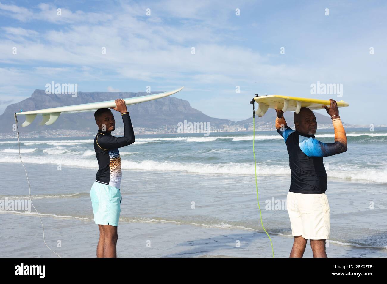 Portrait of african american father and son carrying surfboards on ...