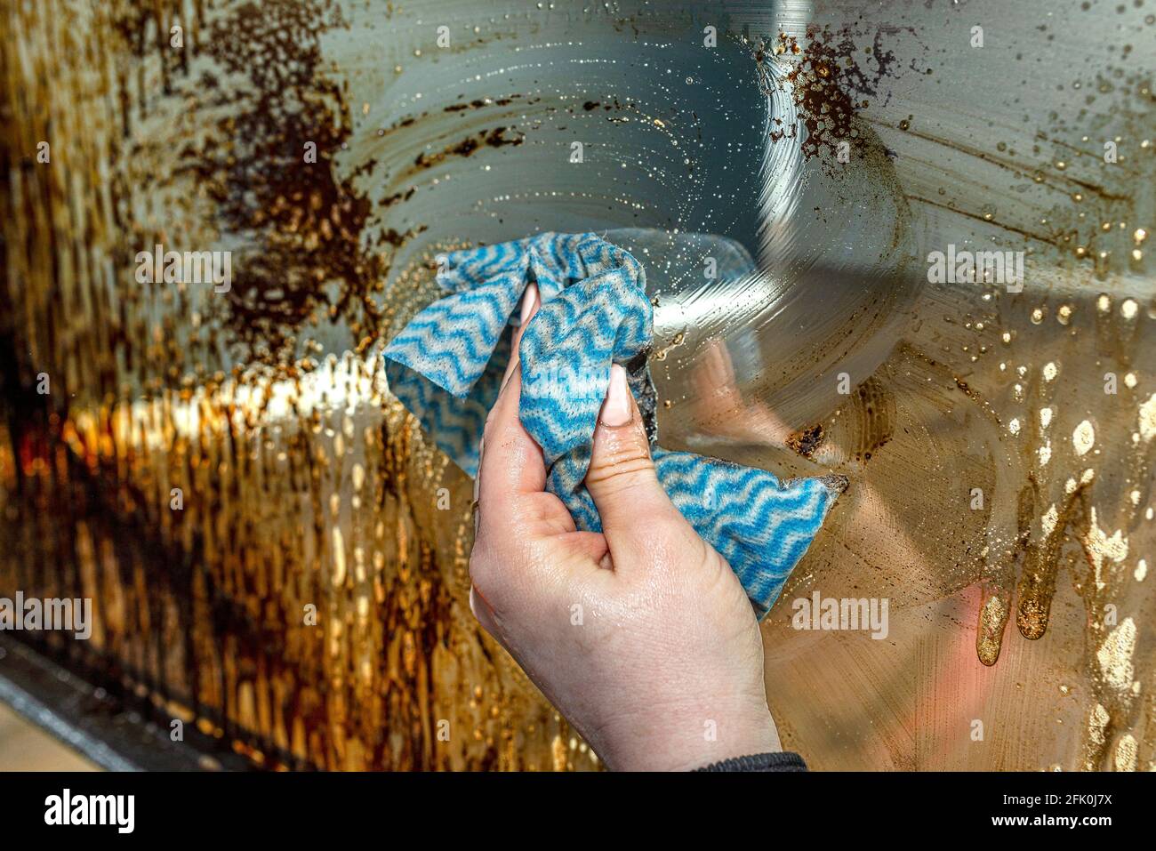A woman washes with a kitchen cloth the corner pane covered with soot ...