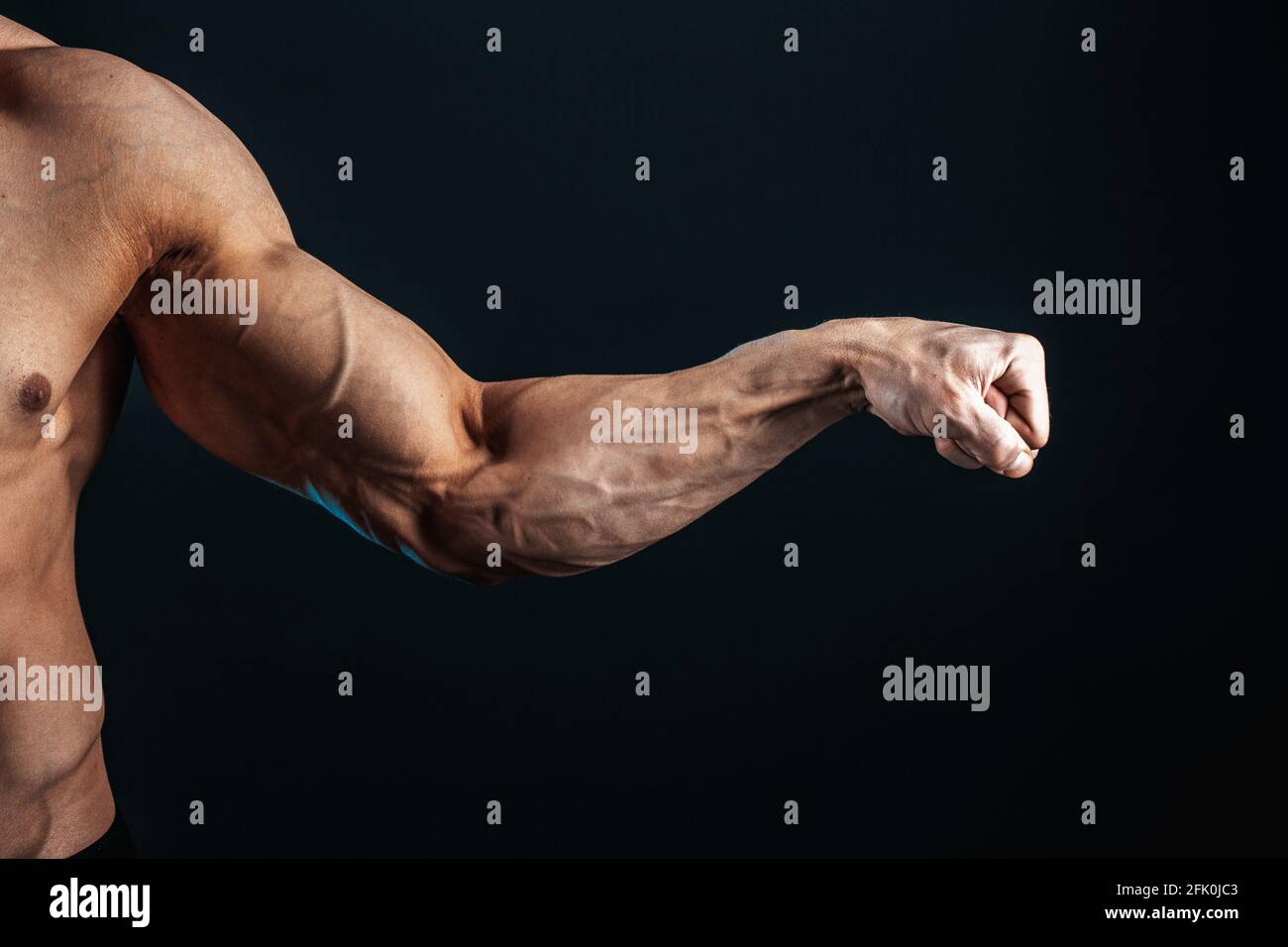 tense arm clenched into fist, veins, bodybuilder muscles on a dark ...