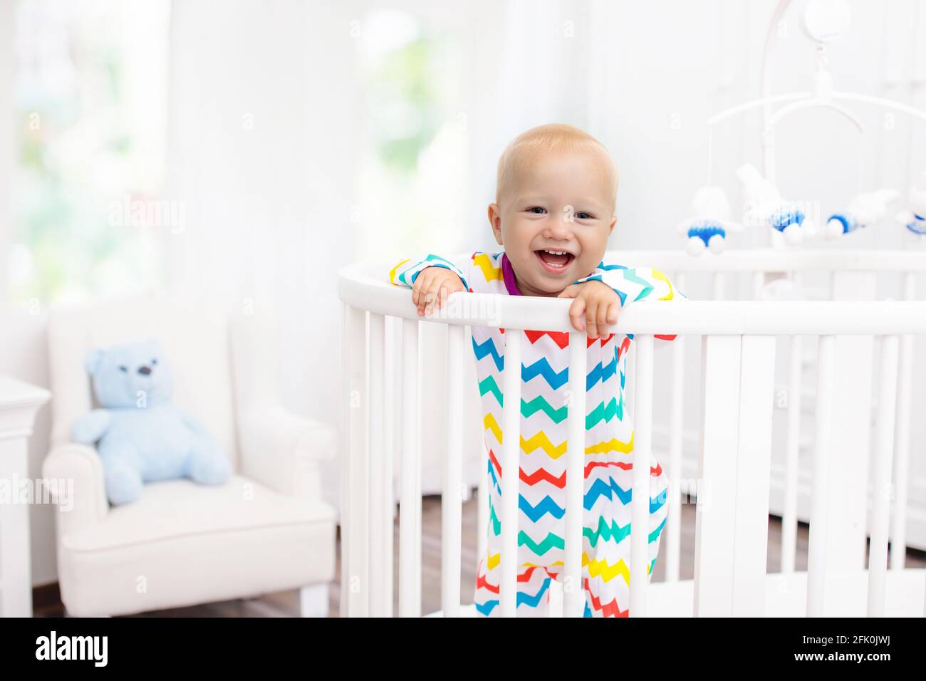 Cute laughing baby standing in bed after nap time. Nursery interior for ...