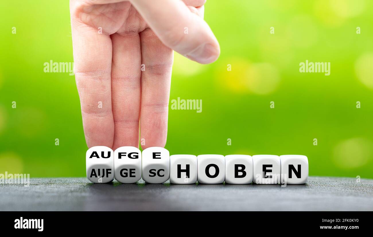 Hand turns dice and changes the German word "aufgeschoben" (postponed ...