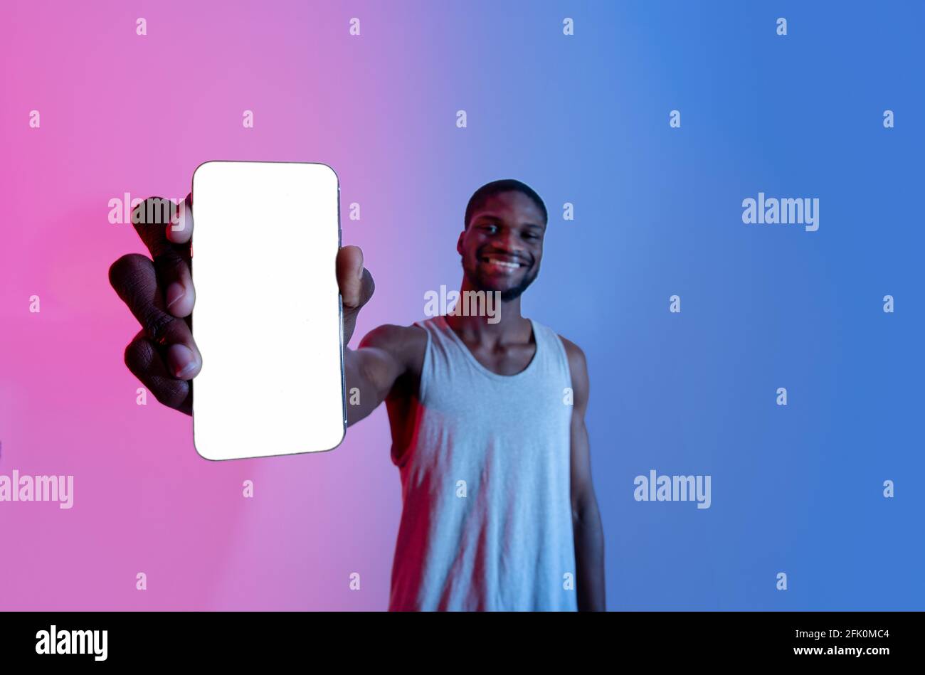 Cheerful black sportsman showing smartphone with empty screen in neon ...