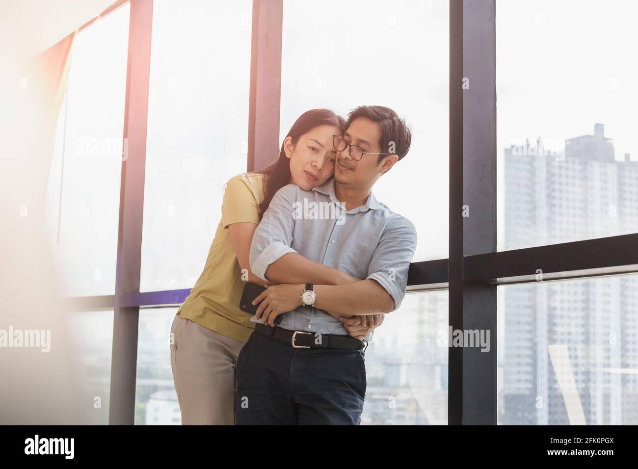 Happy couple cuddling standing next to big window Stock Photo - Alamy