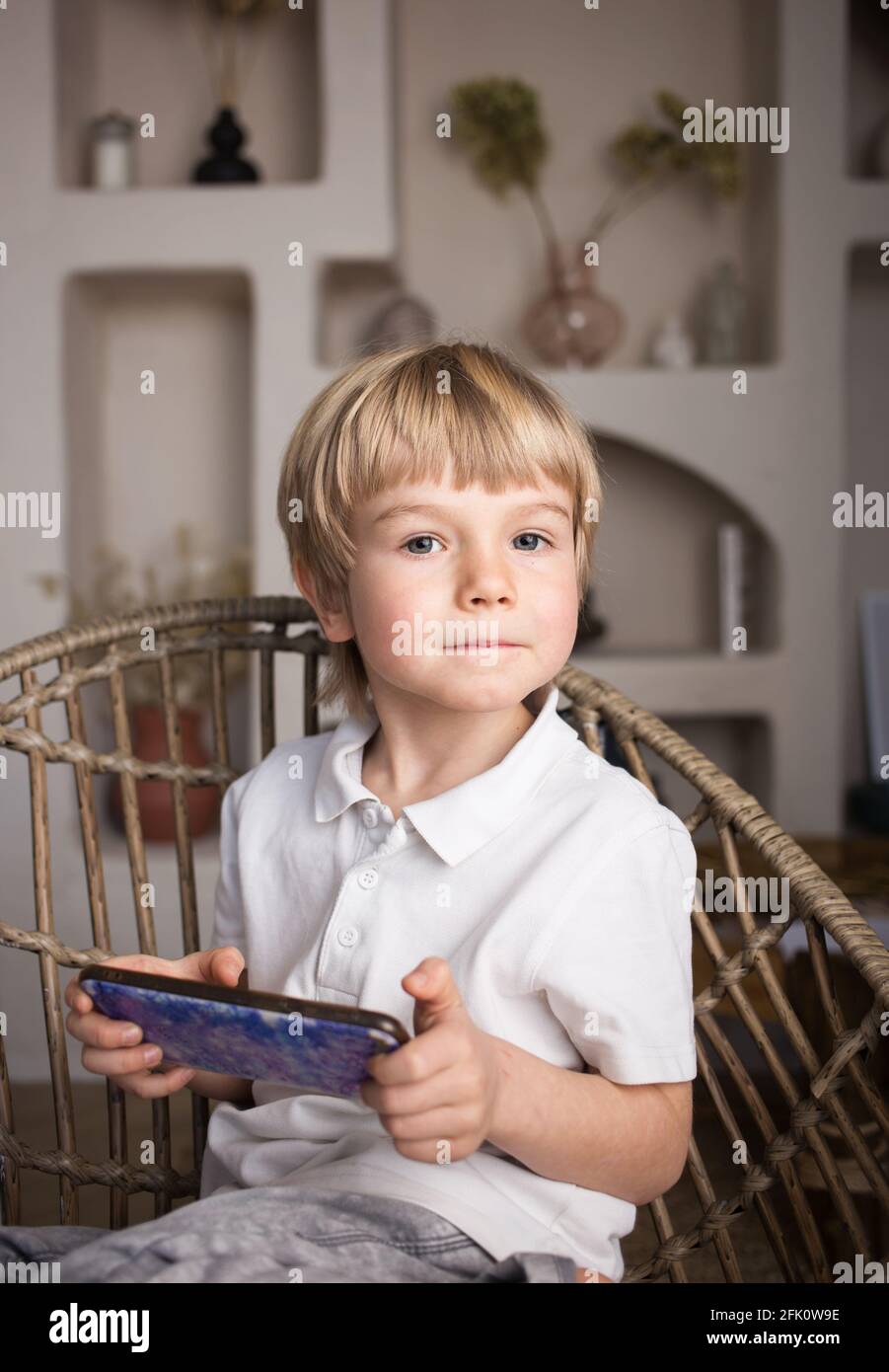 cute toddler boy is sitting in the room and holding a mobile phone in ...