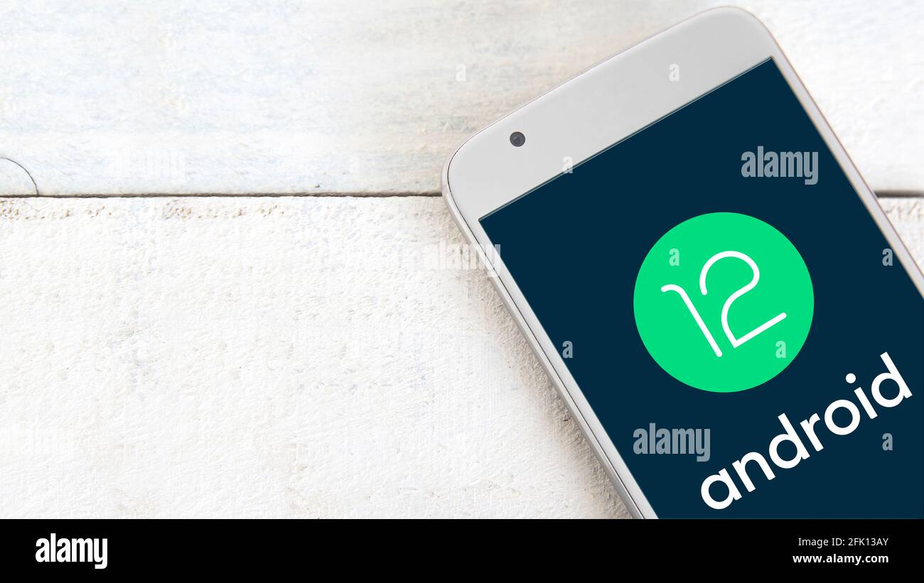 Android 12 logo on a screen of a mobile on a white wooden table. Empty ...