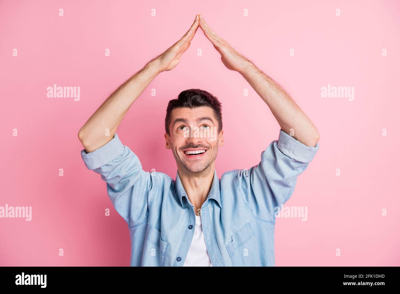 Photo portrait of young man keeping hands over head showing roof moving ...