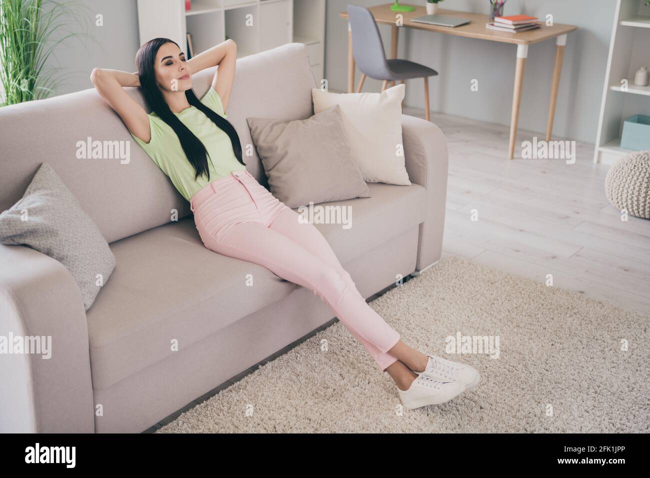Photo of young charming girl sitting sofa hands behind head eyes closed ...