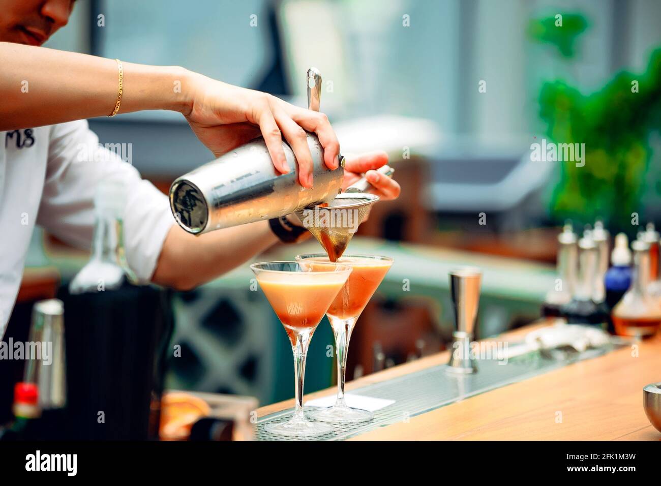 Bartender pouring orange cocktail from mixer to glasses Stock Photo - Alamy