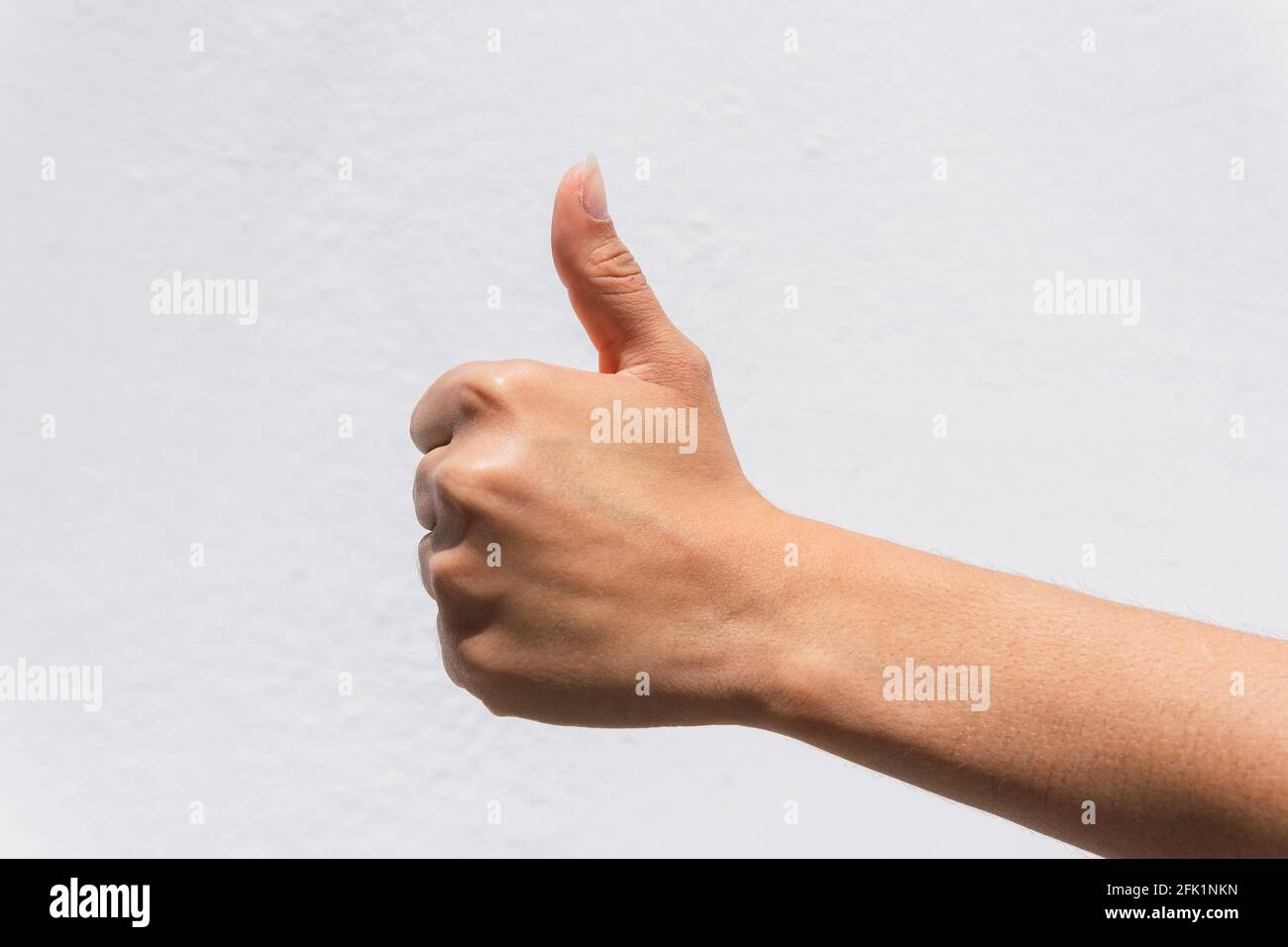 Closeup of thumbs-up hand sign against a white wall background Stock ...