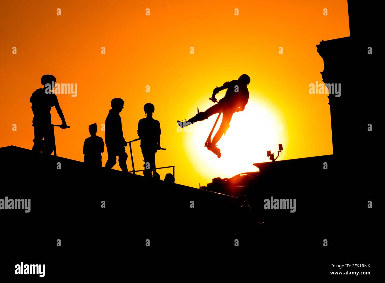 Teenager silhouette showing high jump tricks on scooter against orange ...