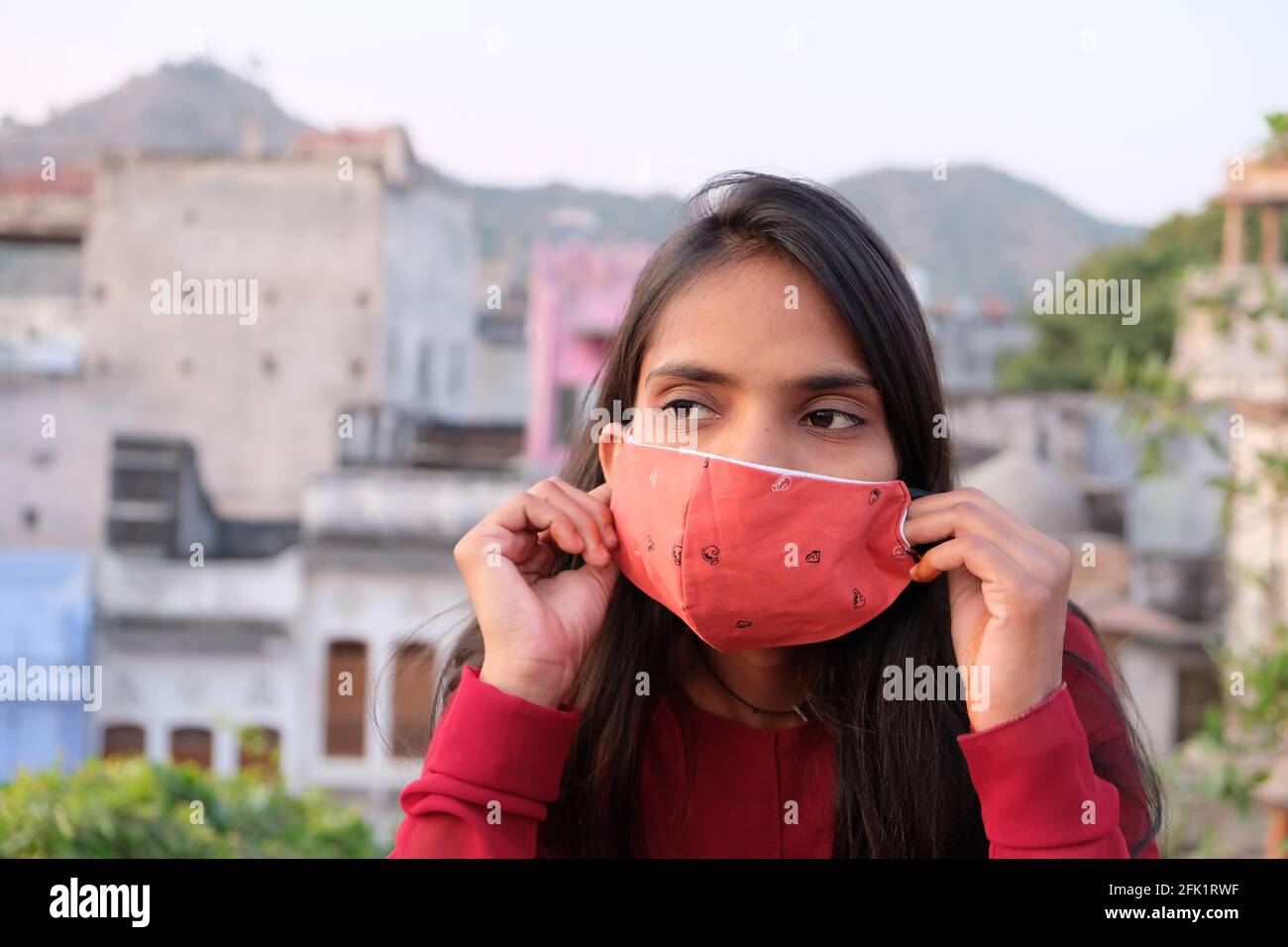 Portrait of a young Indian female putting on a red reusable textile ...