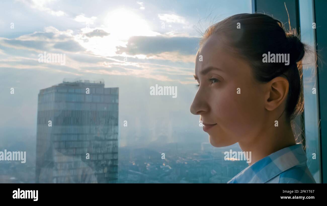 Woman looking at cityscape through window of skyscraper - side view ...
