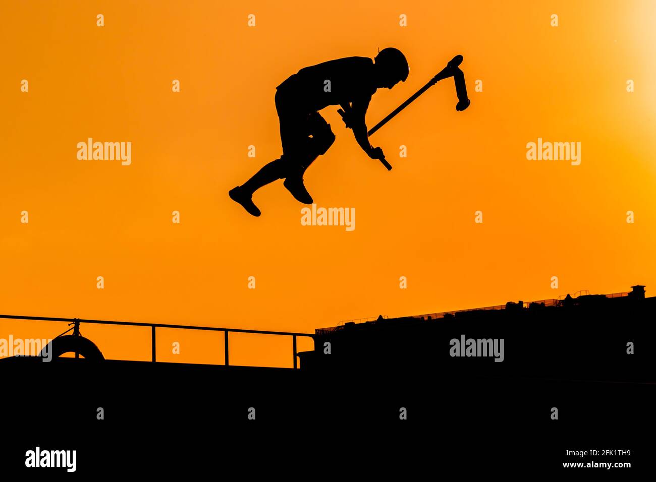 Teenager silhouette showing high jump tricks on scooter against orange ...
