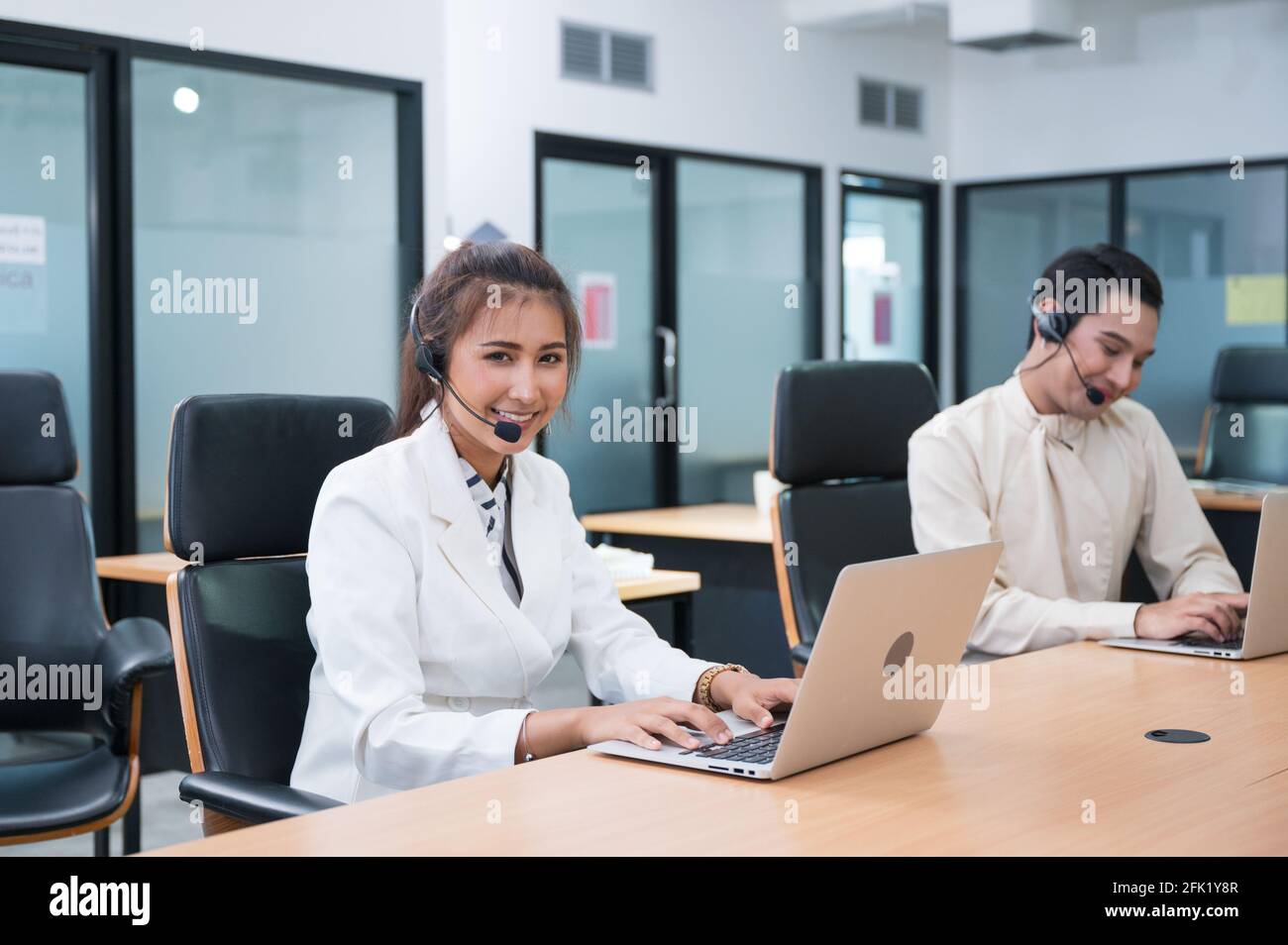Friendly operator asian woman agent with headset working with laptop on customer consultation in ...