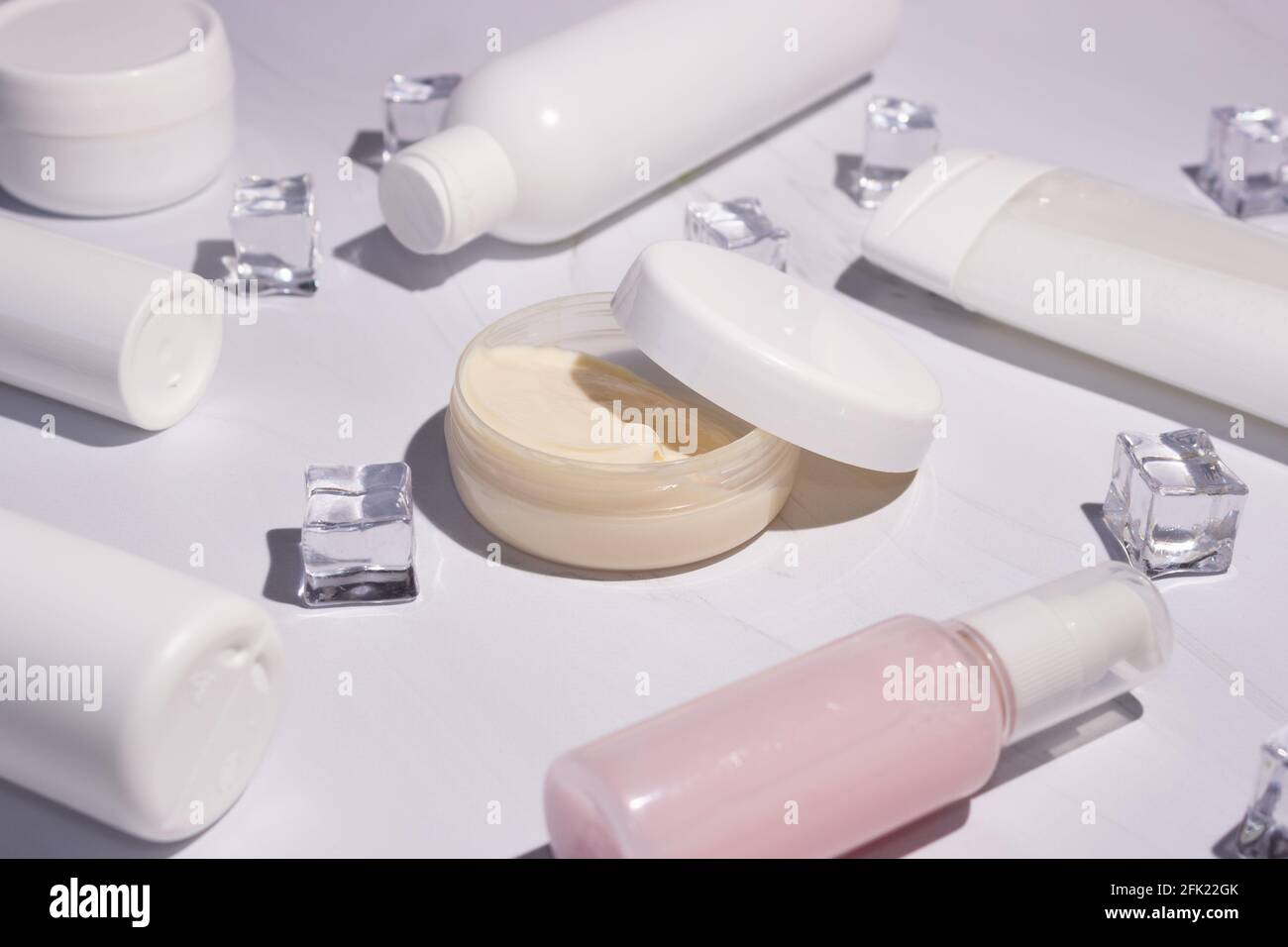 Cream in a jar with an open lid and bottles for cosmetics. Ice cubes ...