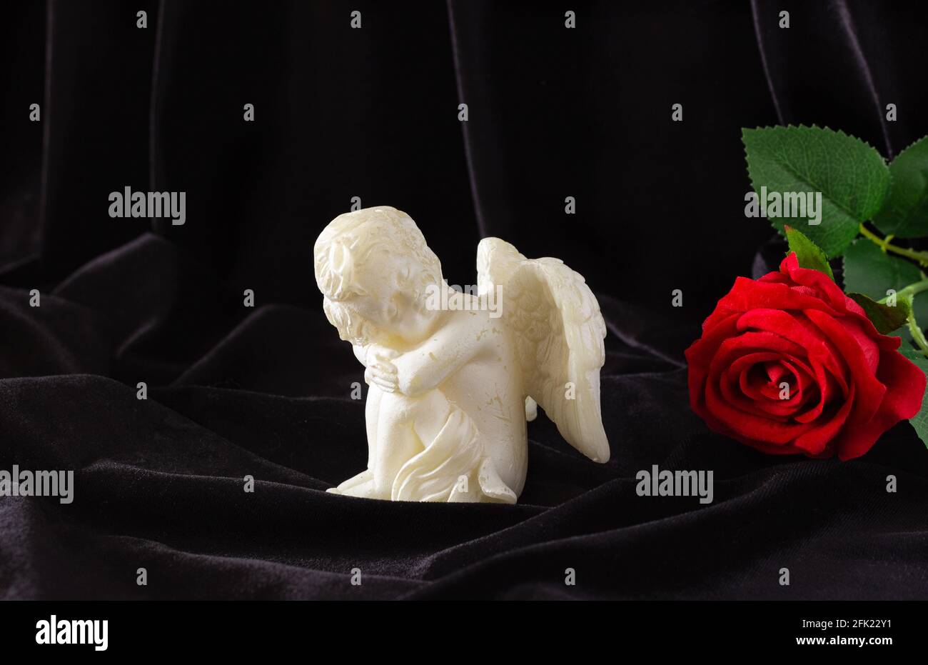 A small sculpture of a baby angel with wings and a red rose on a black ...