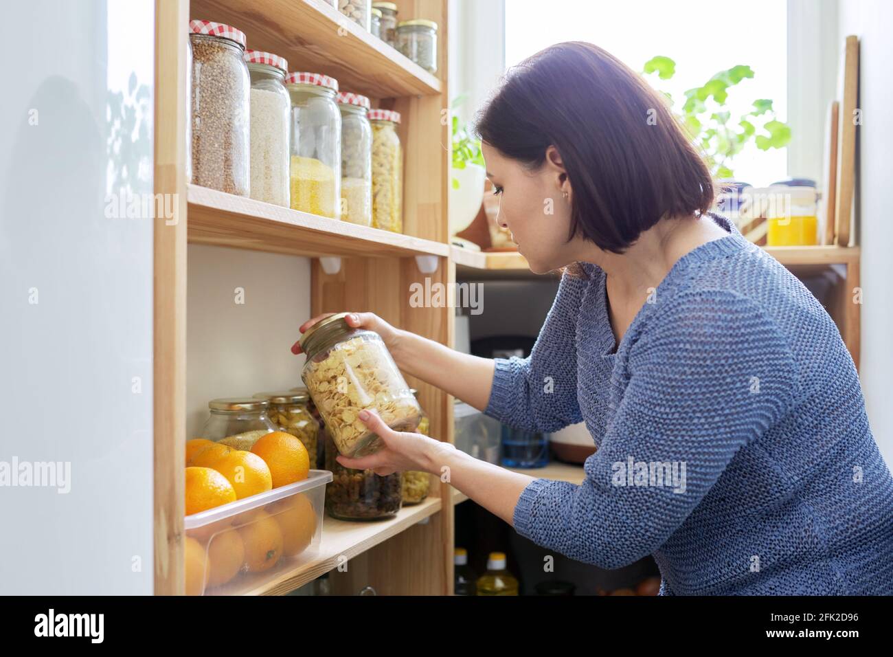 Organization of pantry, woman in kitchen near wooden rack with cans and ...