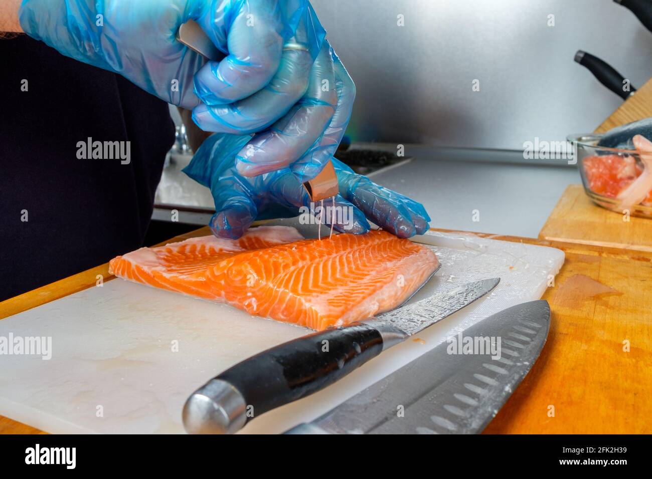 A cook wearing hygienic gloves uses special fish tweezers to remove ...